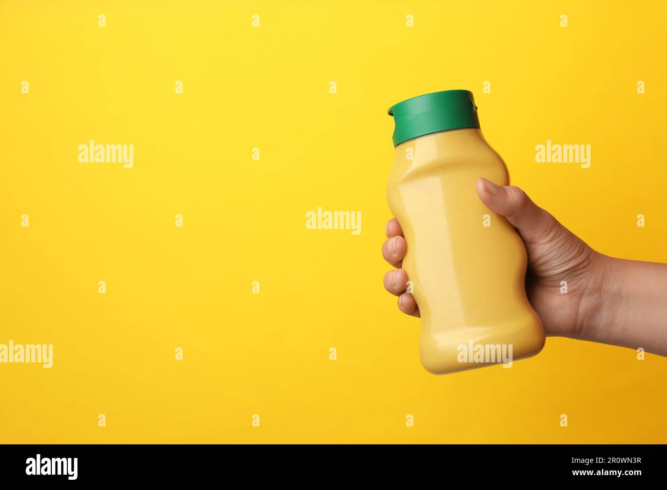 Woman with bottle of mustard on yellow background, closeup. Space for ...