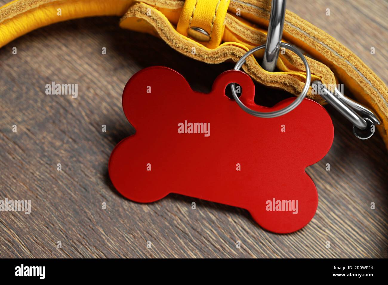 Yellow leather dog collar with red tag in shape of bone on wooden table ...
