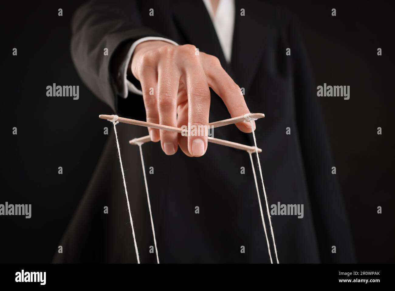 Woman in suit pulling strings of puppet on black background, closeup ...