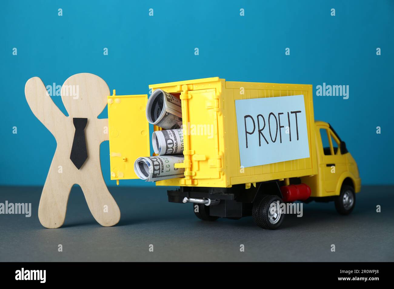 Economic profit. Wooden figure and toy truck with banknotes on grey ...