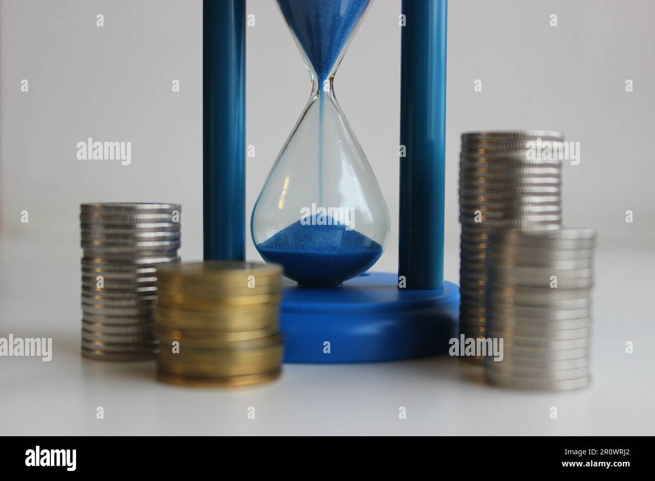 Falling blue sand in an sand glass surrounded by columns of coins ...