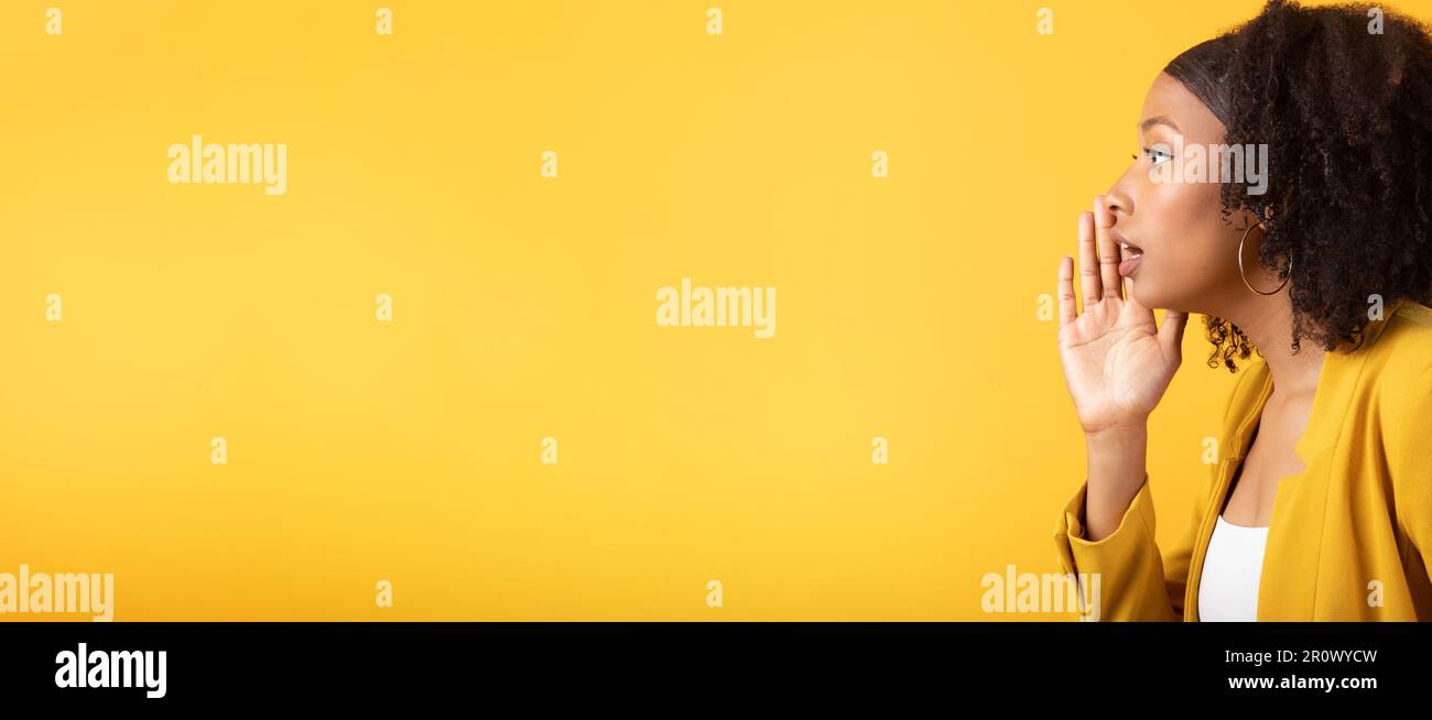 Black lady whispering secret, pressing hand to face, isolated on yellow ...