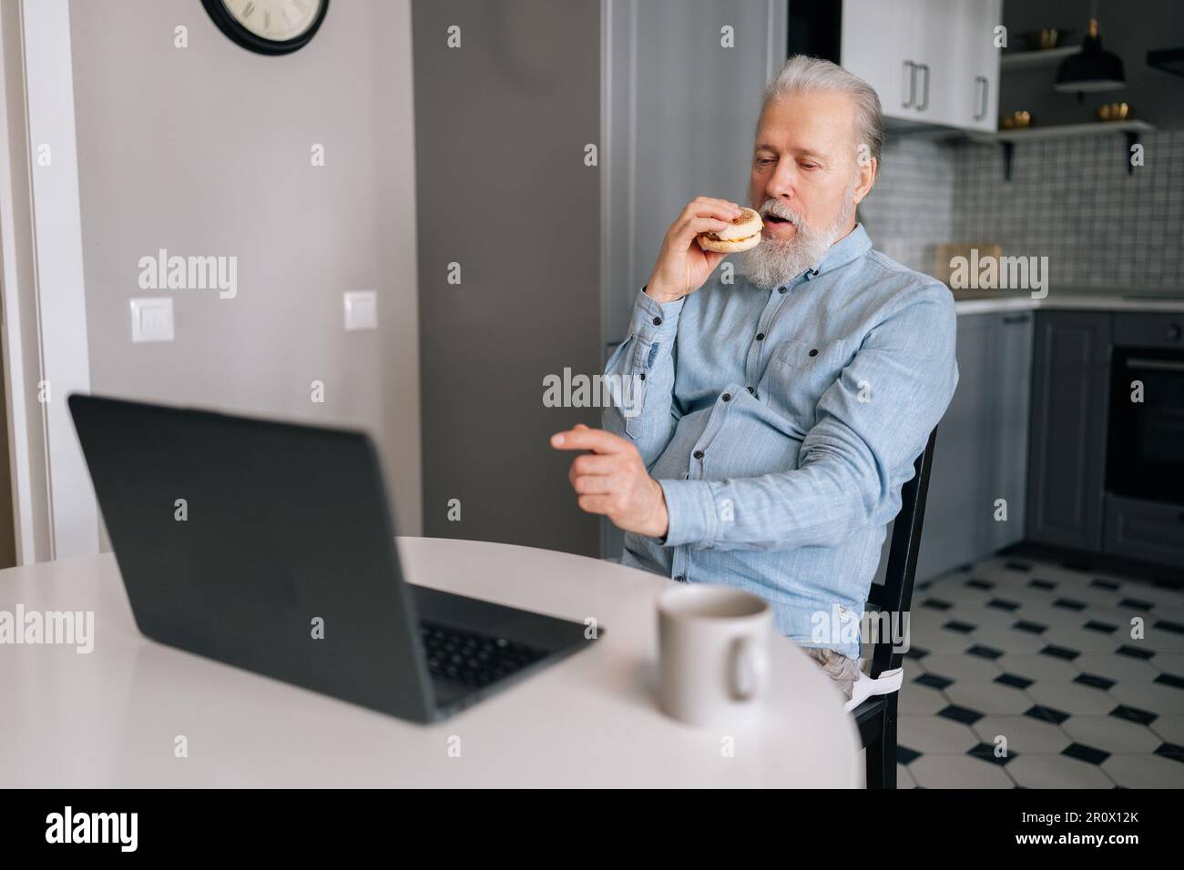 Hungry bearded senior older businessman eating hamburger with beef from ...