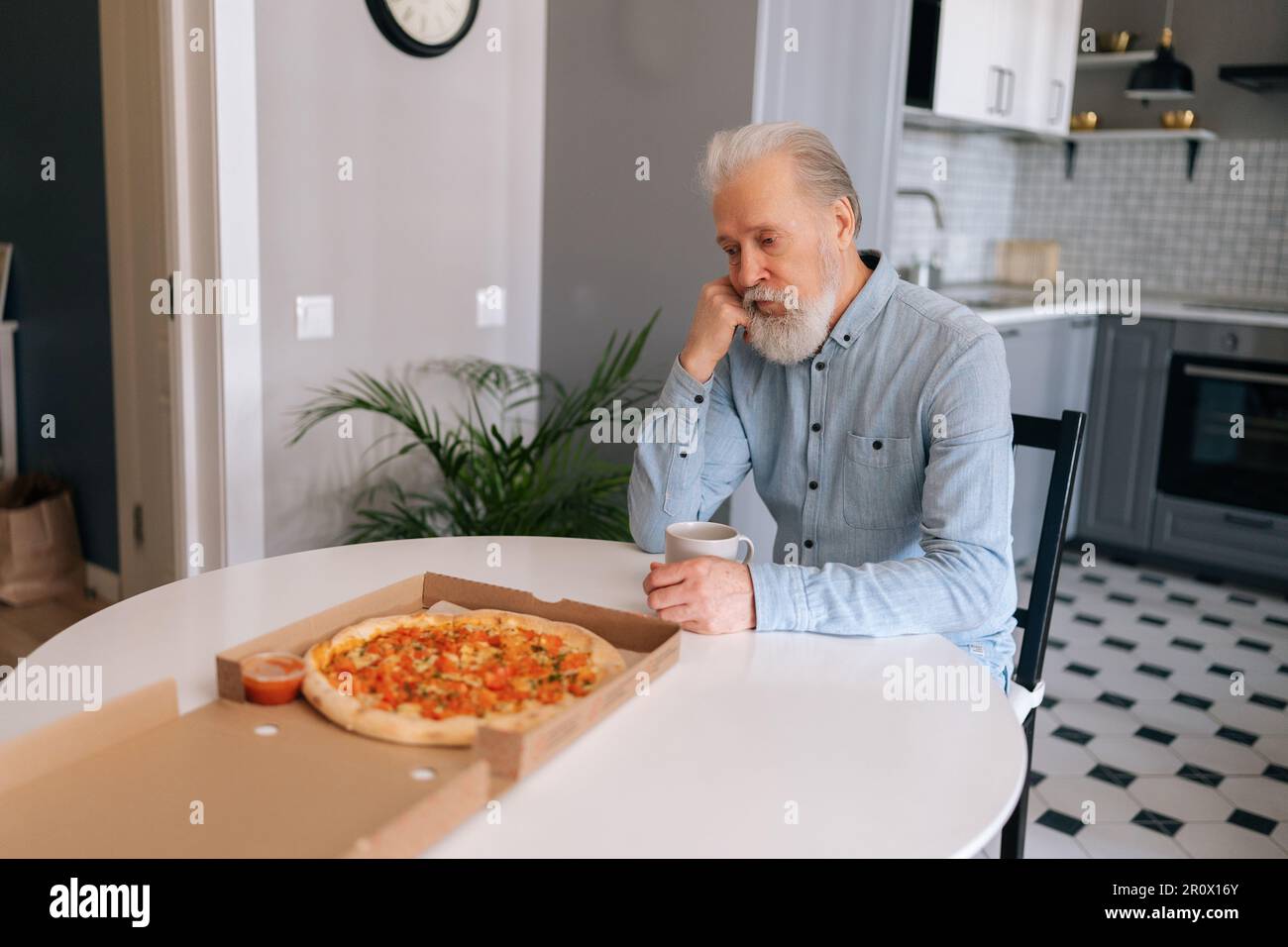 Portrait of gray-haired mature adult male eating tasty pizza thinking ...