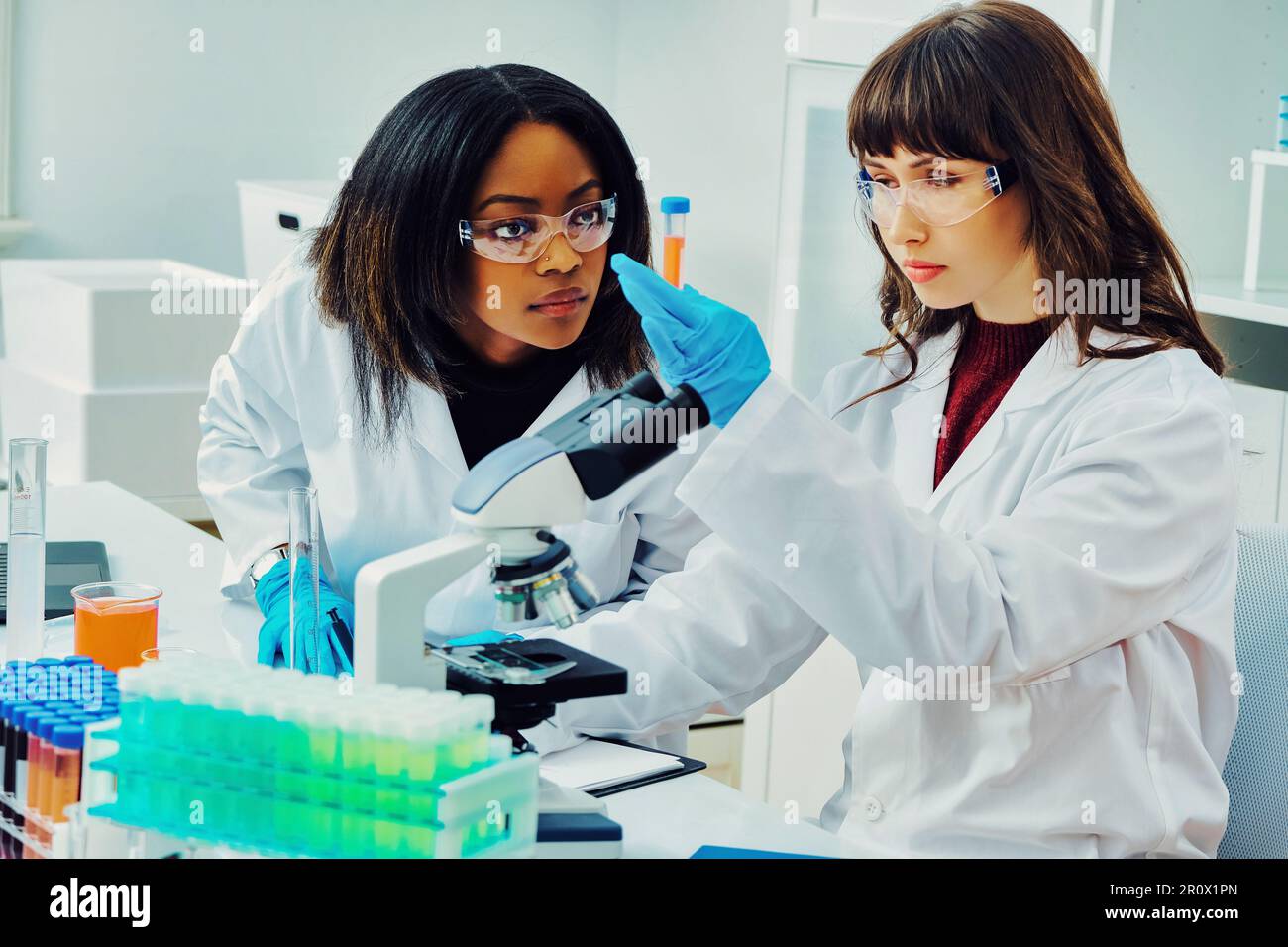 Two young women wearing lab coats working in hospital, looking at test ...