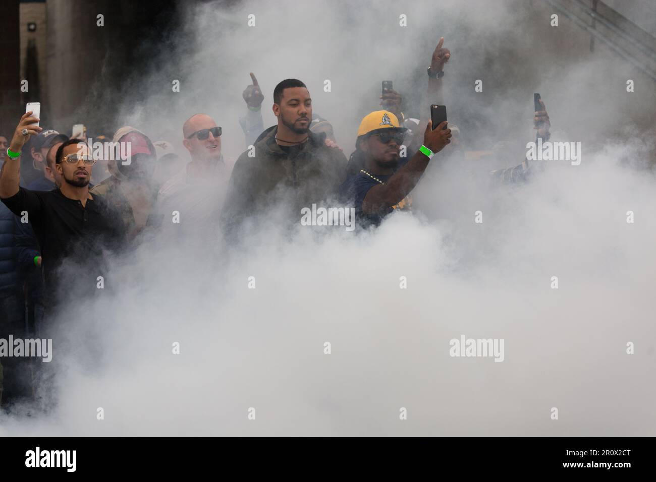 A crowd of people standing in a smoky street, holding a mobile phone in ...
