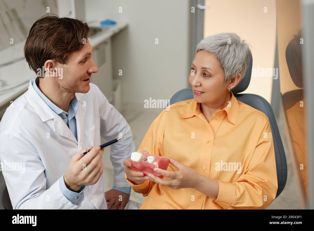 Side view portrait of smiling male dentist talking to senior woman in ...