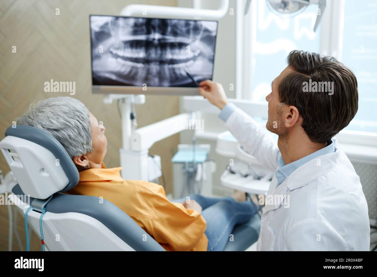 Back view of male dentist pointing at tooth X-ray image on screen ...