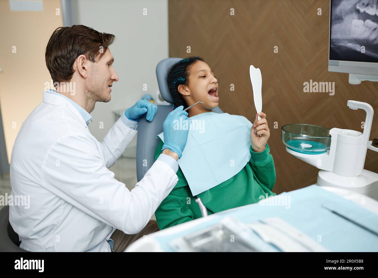 Side view portrait of black teenage girl looking in mirror during dental checkup in clinic Stock ...
