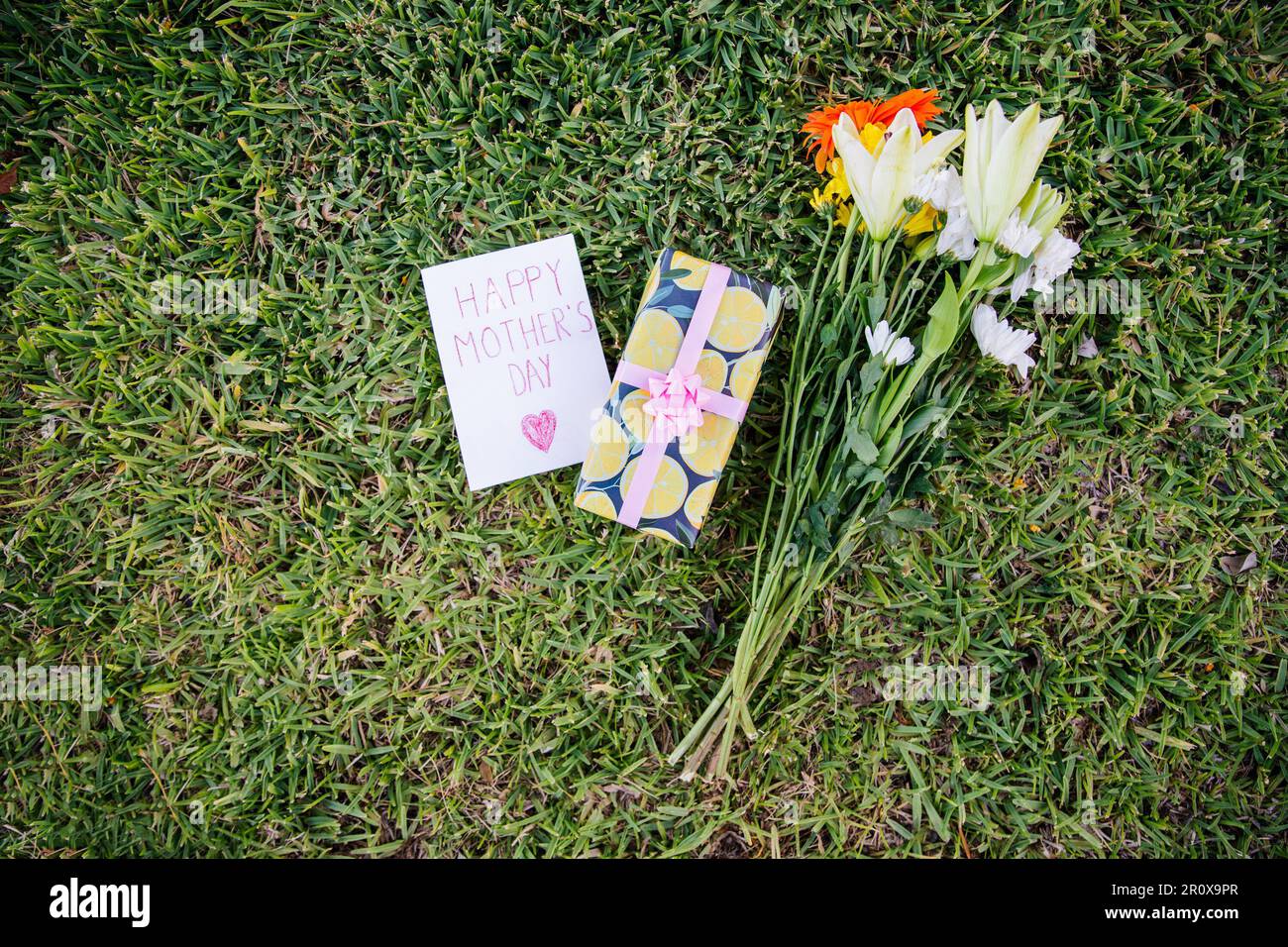 Bunch of flowers, gift and dedication card resting on a lawn for Mother ...