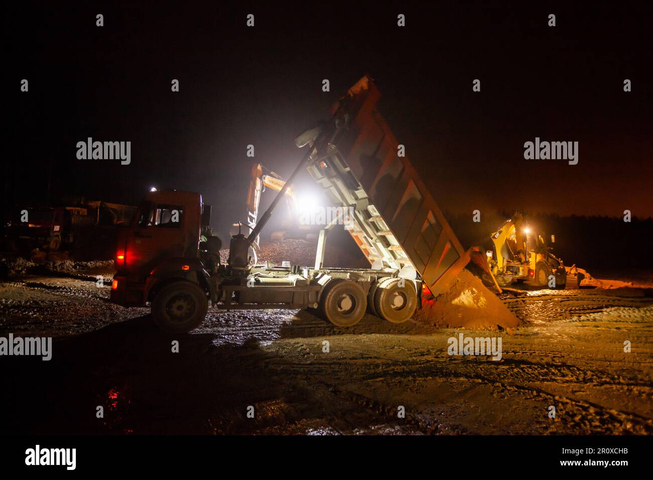 Road construction site at night. Excavator moves gravel. Dump truck ...