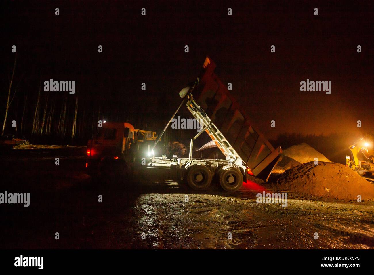 Road construction site at night. Excavator moves gravel. Dump truck ...