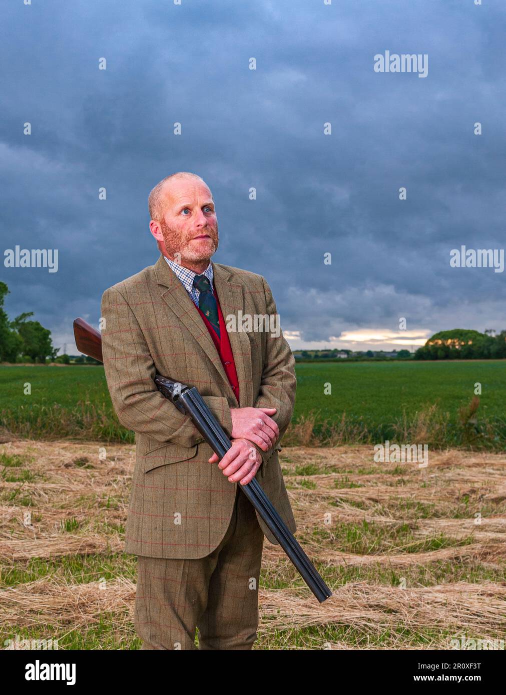 An English gentleman stood at twilight in a tweed shooting suit with a ...