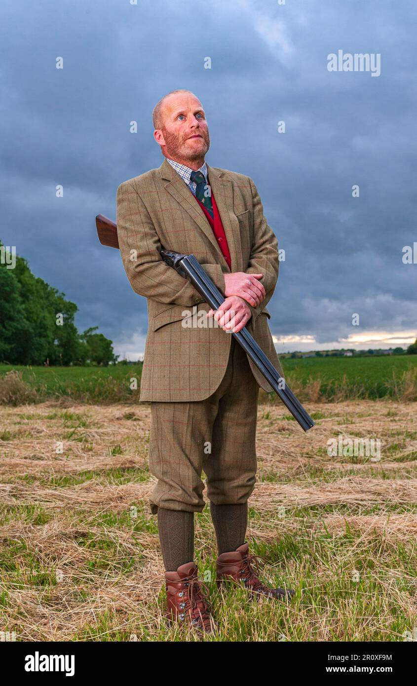 An English gentleman stood at twilight in a tweed shooting suit with a ...