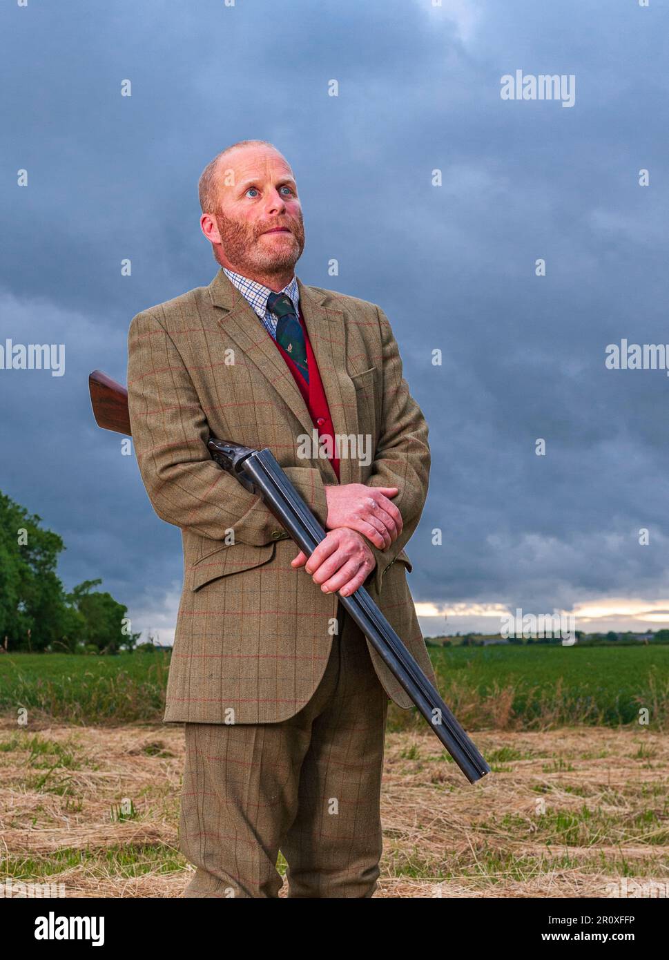 An English gentleman stood at twilight in a tweed shooting suit with a ...