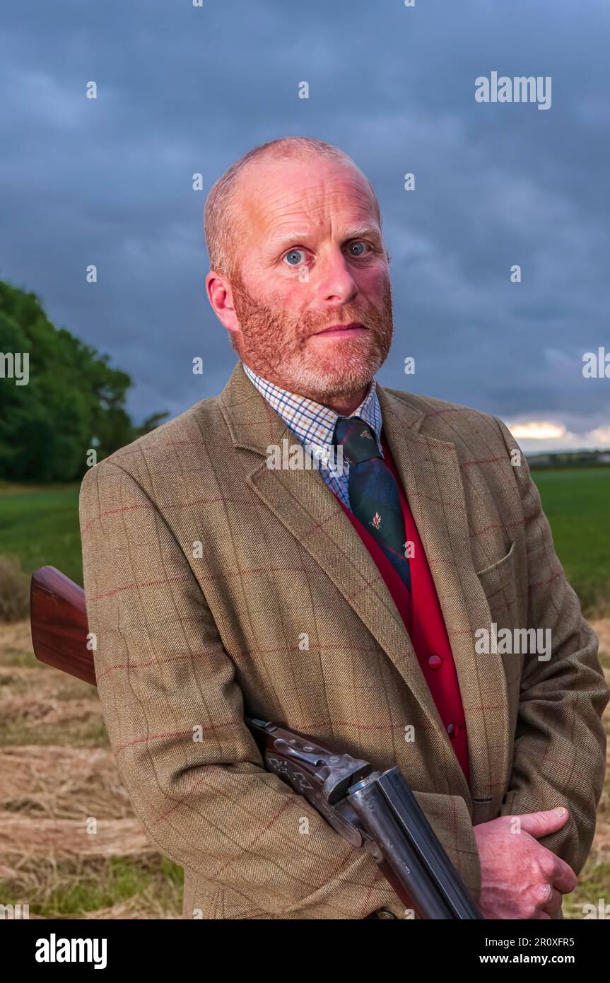 An English gentleman stood at twilight in a tweed shooting suit with a ...