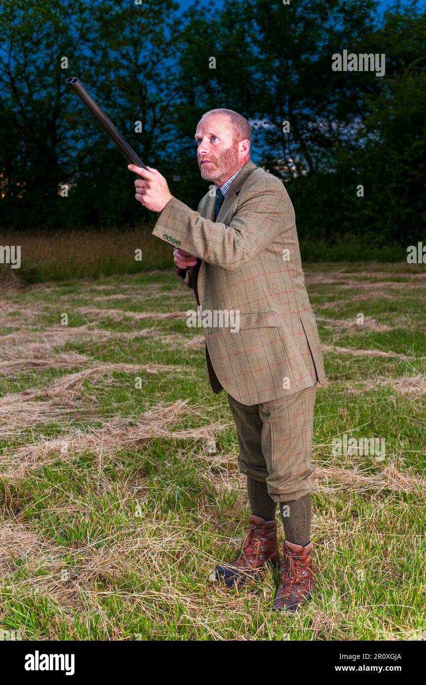 An English gentleman stood at twilight in a tweed shooting suit with a ...