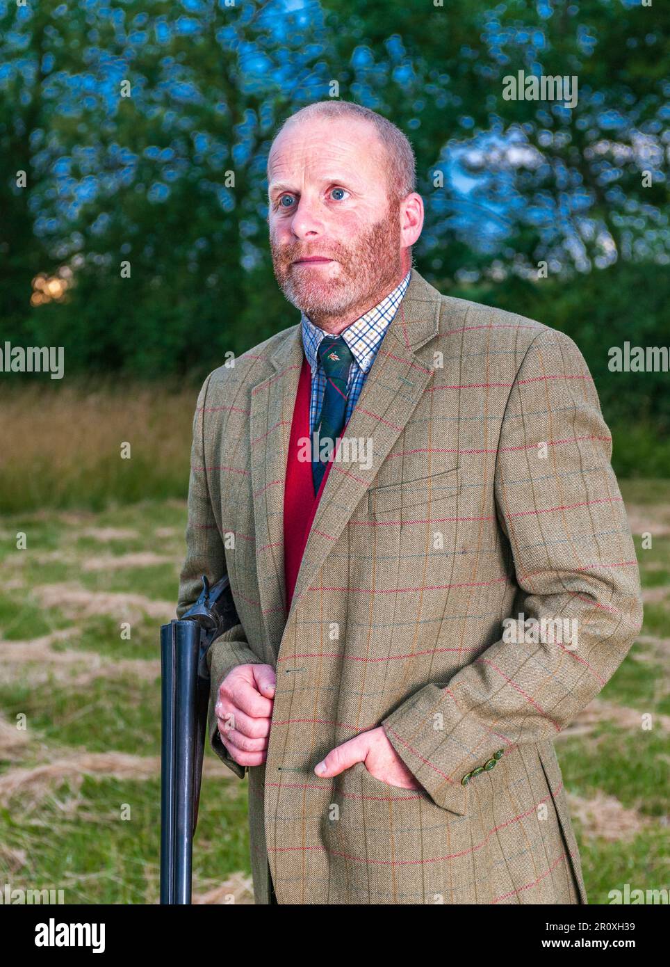 An English gentleman stood at twilight in a tweed shooting suit with a ...