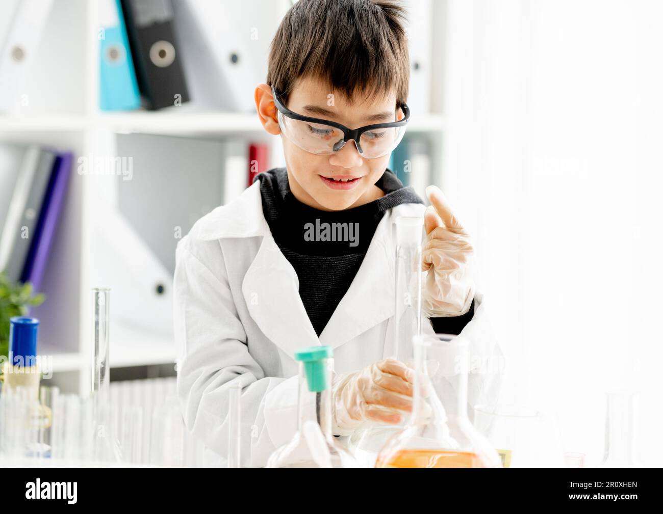 School boy wearing protection glasses doing chemistry experiment in ...