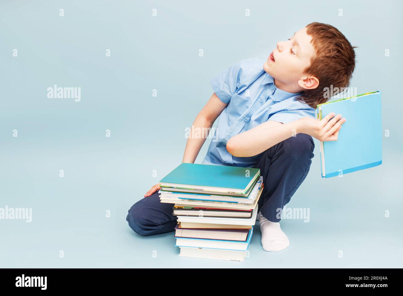 Upset schoolboy sitting with pile of school books and throwing a ...