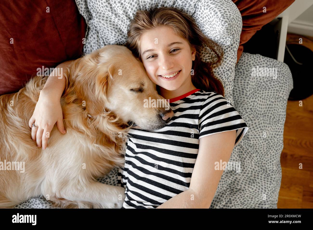 Pretty girl hugging golden retriever dog and lying in bed. Female ...