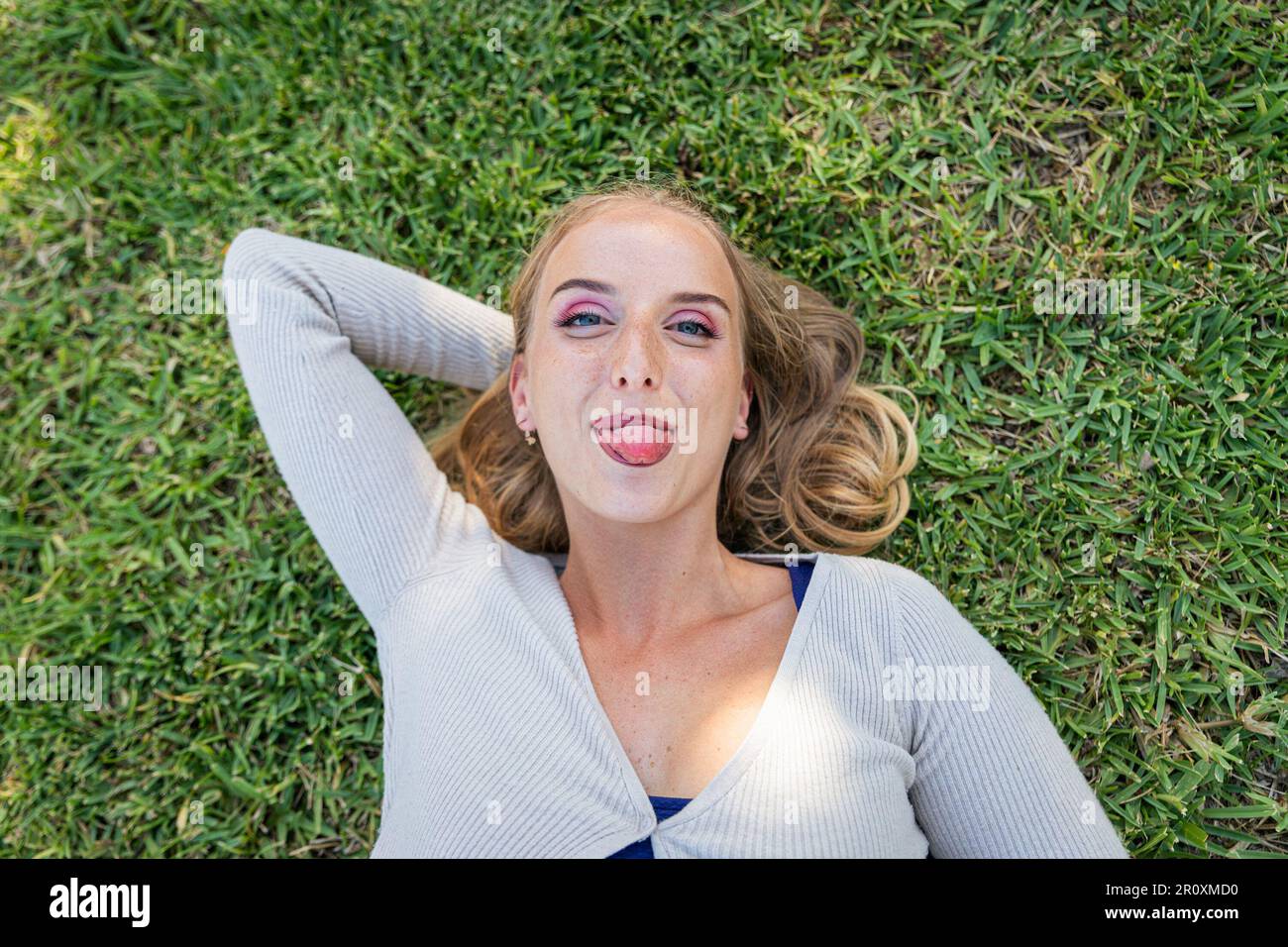 A girl lying on a meadow with an amused expression sticks her tongue ...