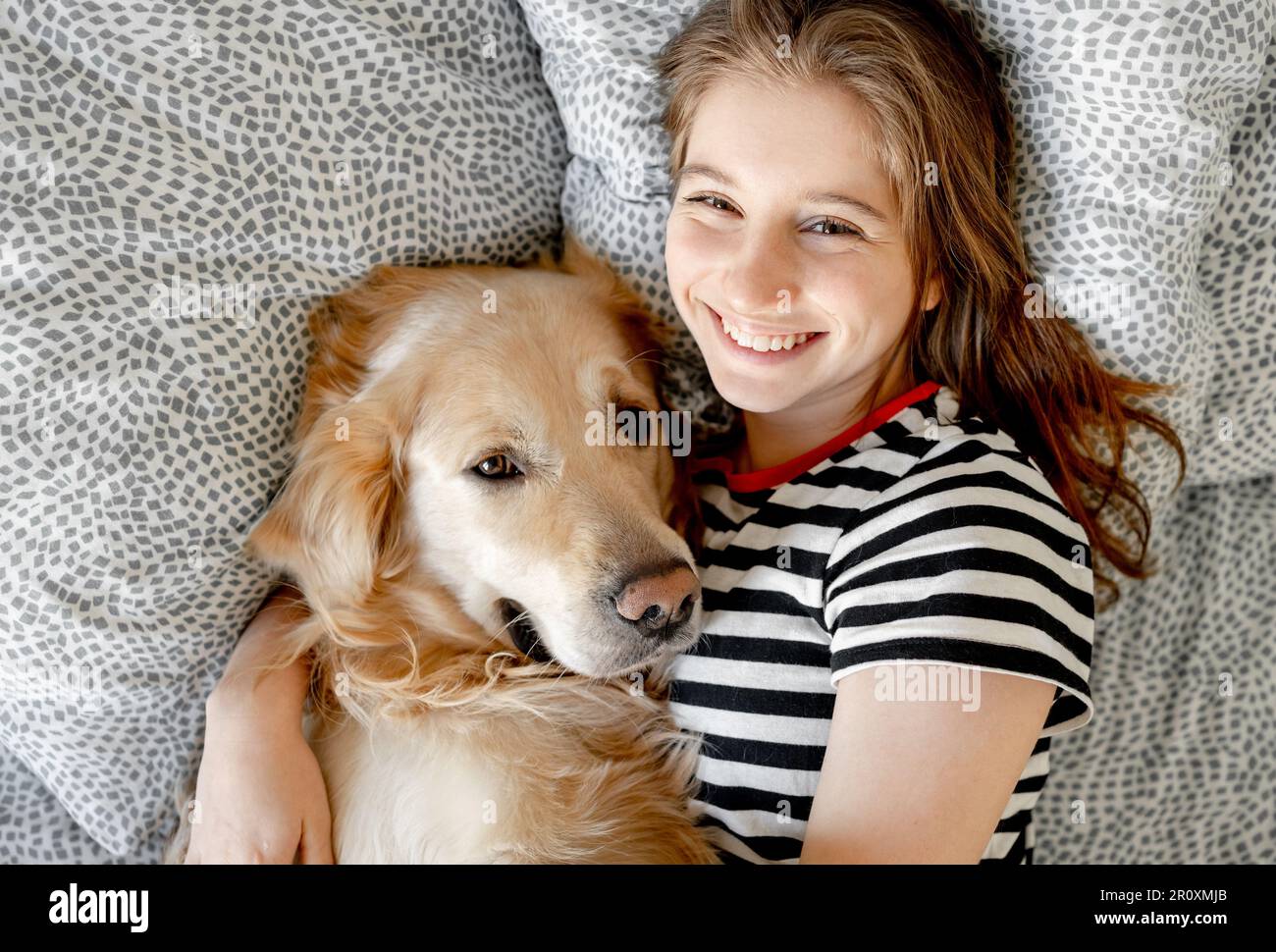 Pretty girl hugging golden retriever dog and smiling lying in bed ...