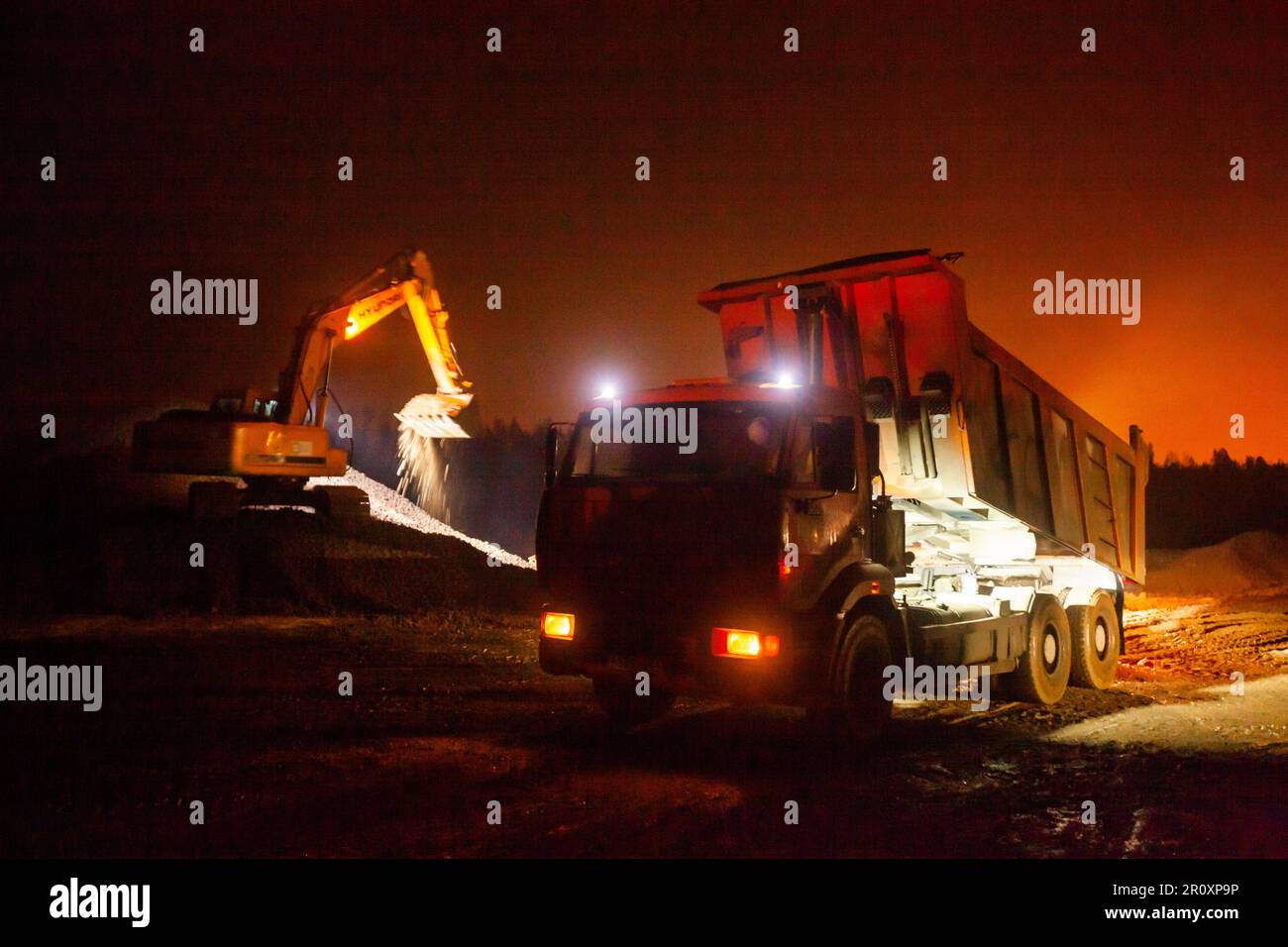 Road construction site at night. Excavator moves gravel. Dump truck ...