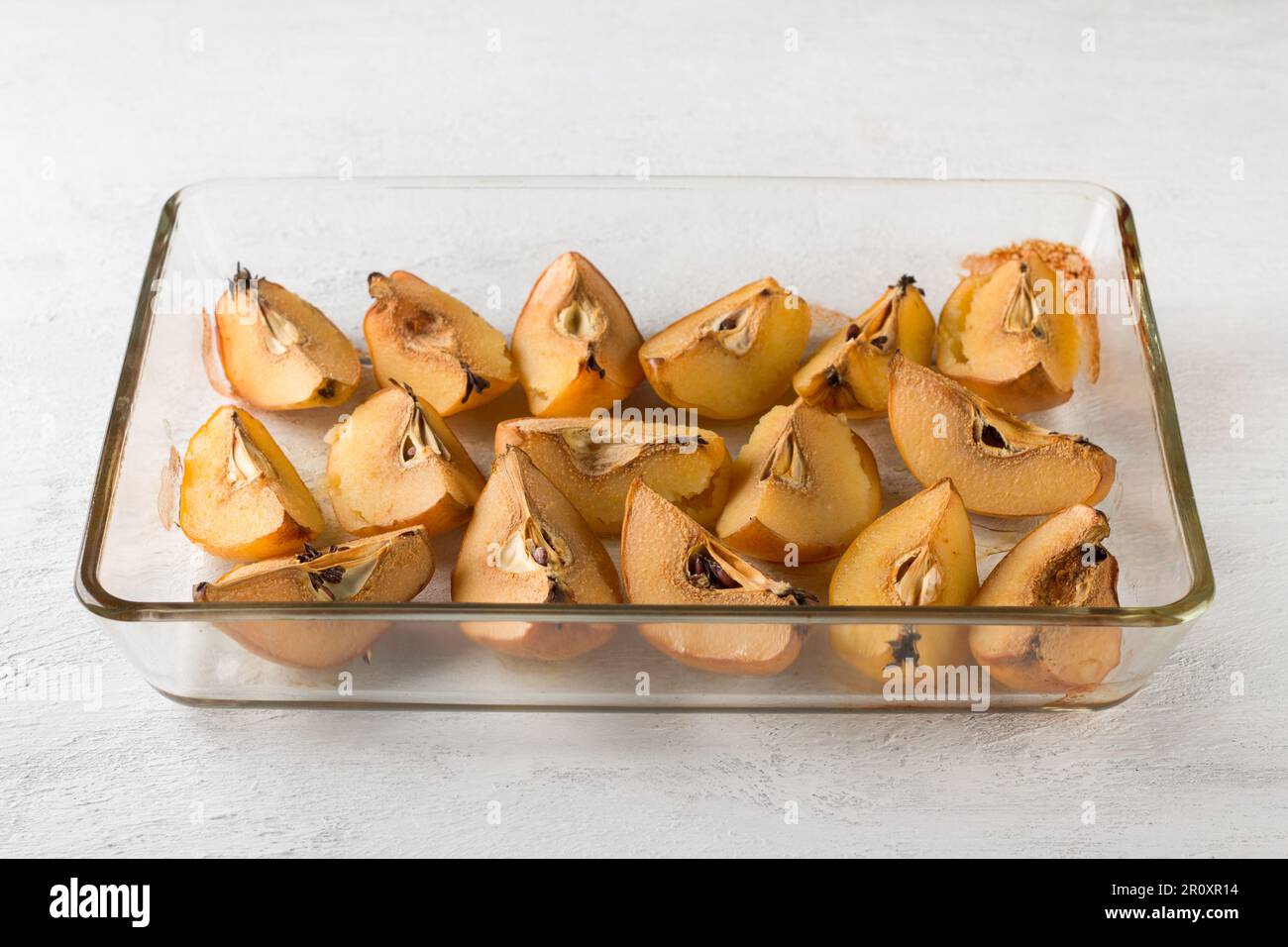 Quartered quince baked in a glass form on a light gray background ...