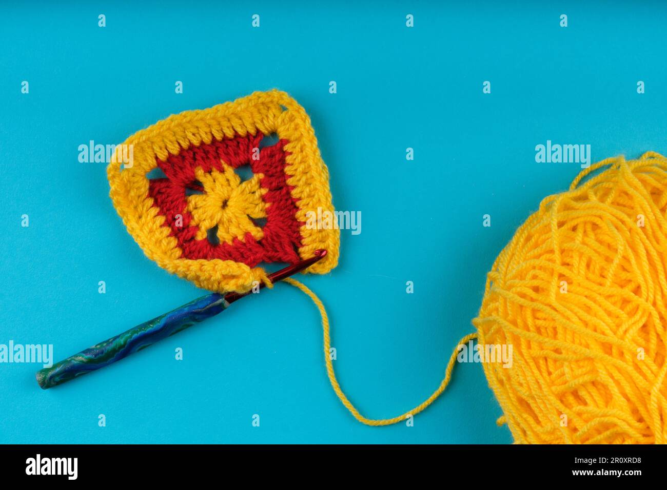 Granny square in yellow and red being crocheted, with a ball of yarn in ...