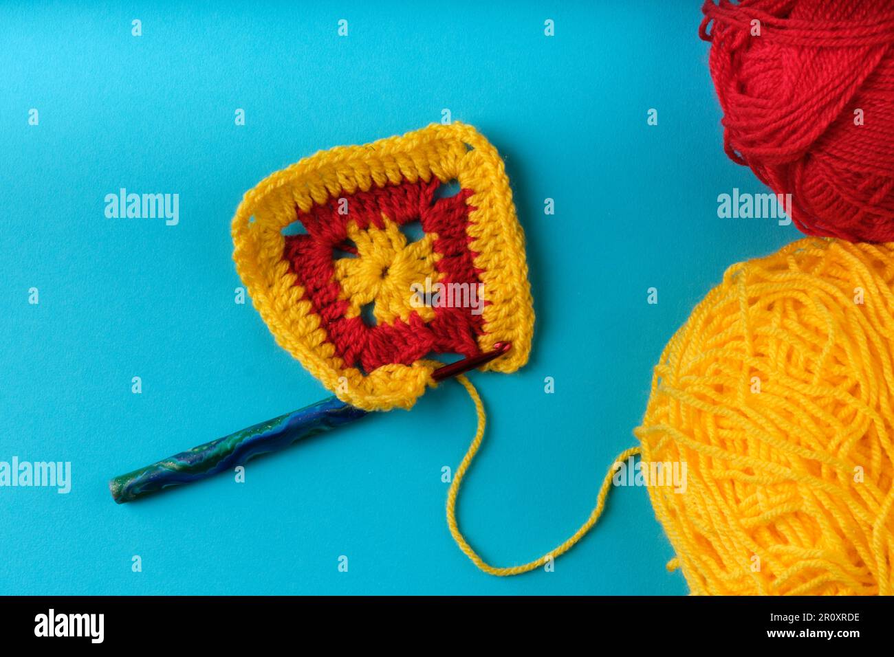 Granny square in yellow and red being crocheted, with two balls of yarn ...