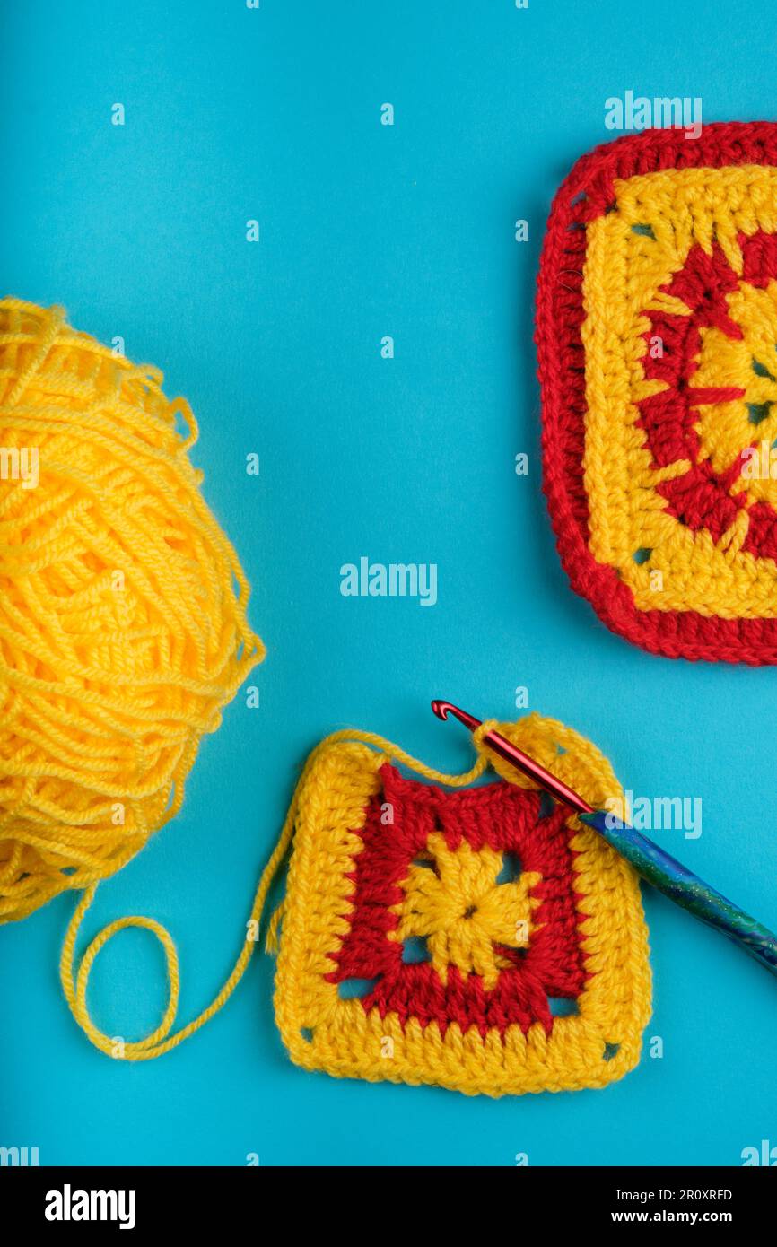 Granny square in yellow and red being crocheted, with a second granny ...
