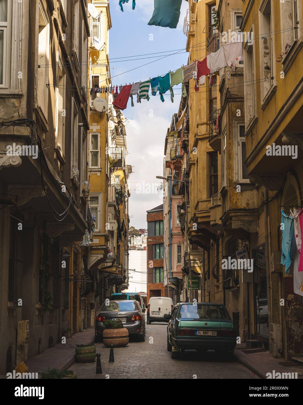 A quaint cobblestone street lined with parked vehicles, with a group of ...