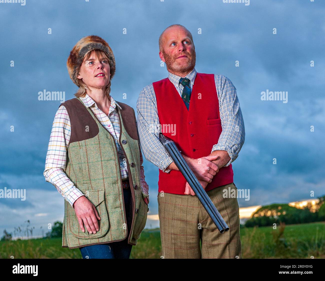 An English lady and gentleman stood at twilight in shooting suits with ...