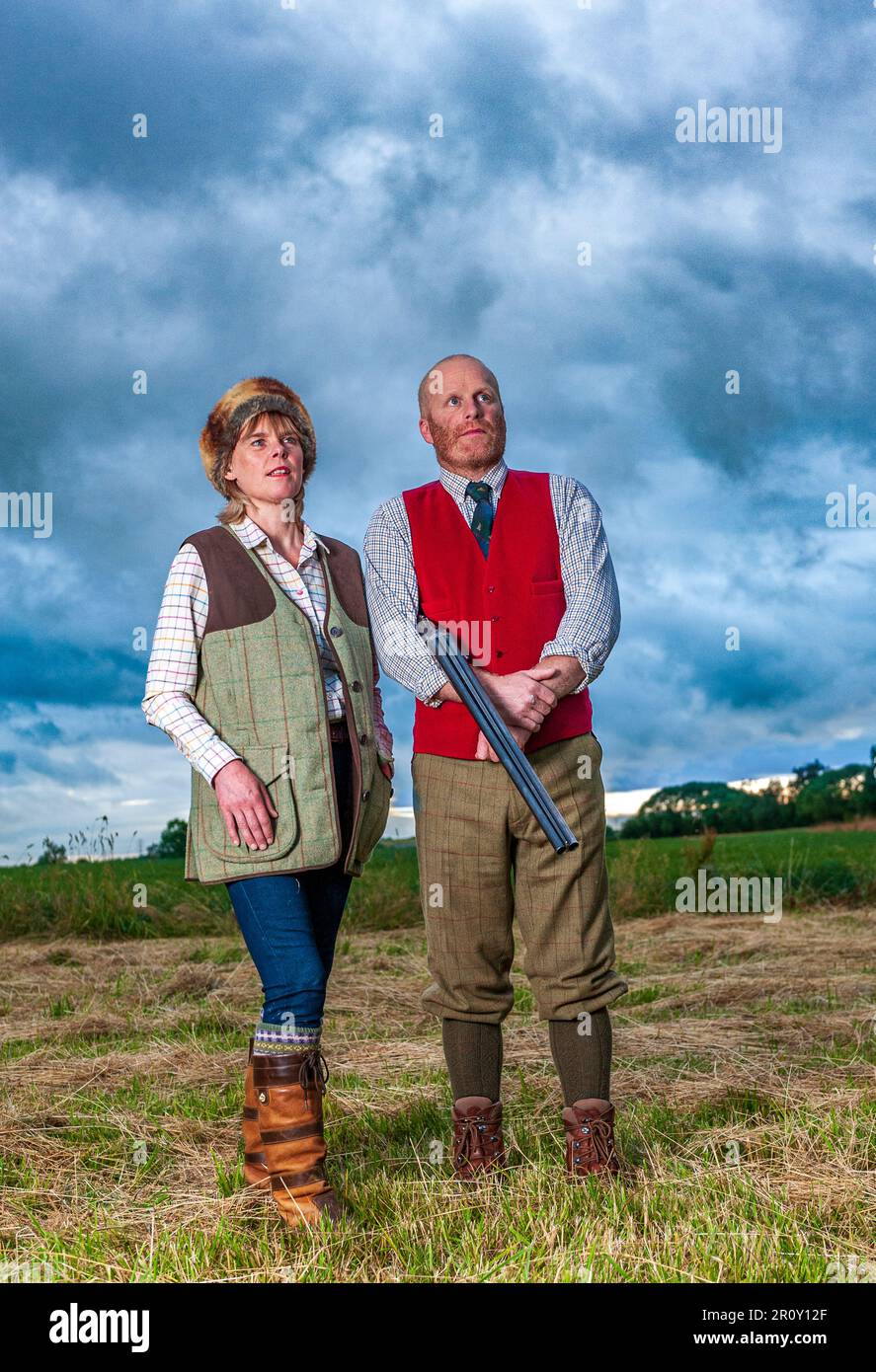 An English lady and gentleman stood at twilight in shooting suits with ...