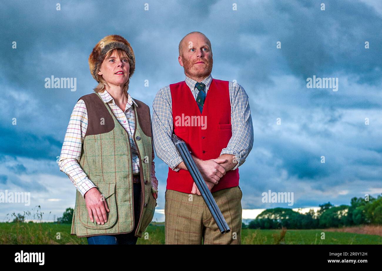 An English lady and gentleman stood at twilight in shooting suits with ...