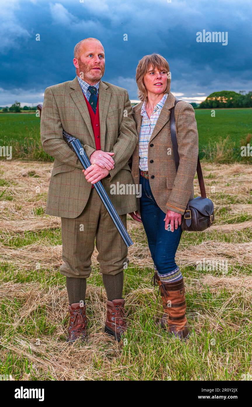 An English lady and gentleman stood at twilight in shooting suits with ...