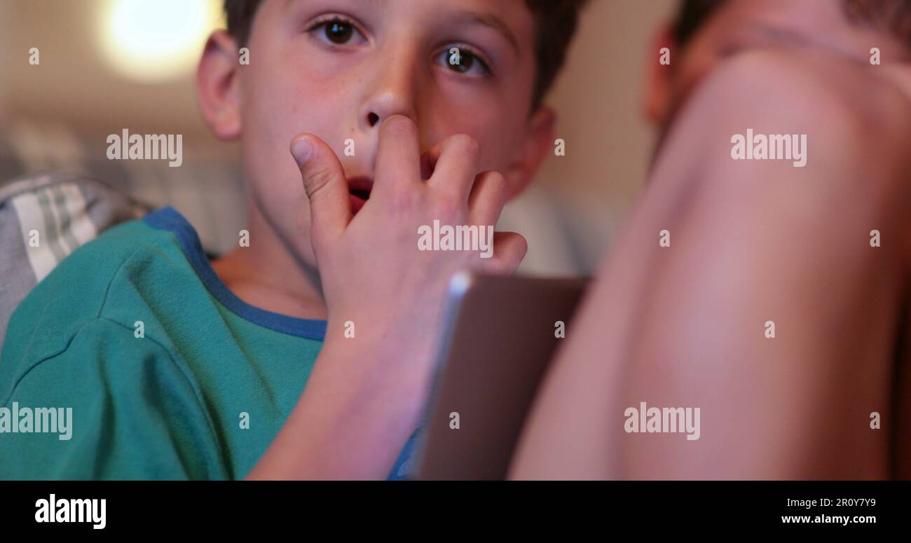 Candid child at home staring at screen holding tablet device. Candid ...