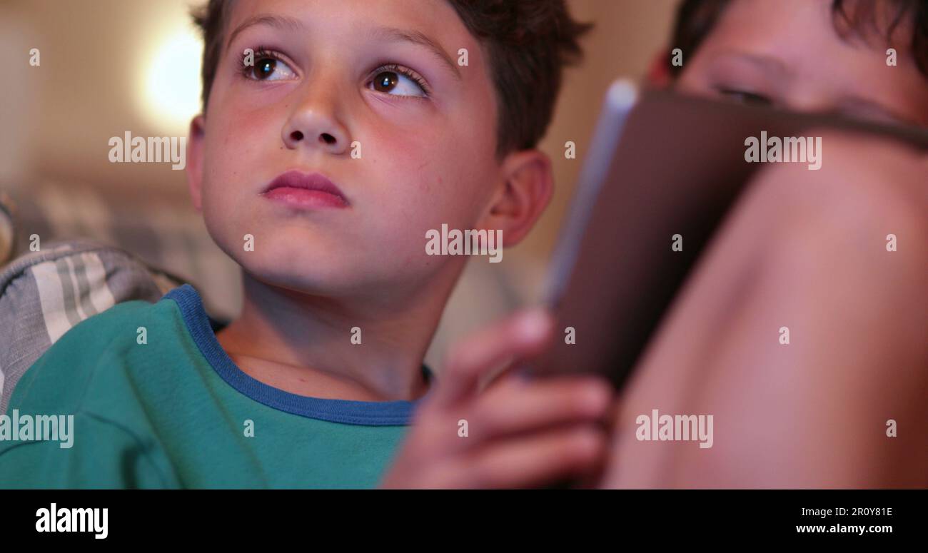 Candid child at home staring at screen holding tablet device. Candid ...