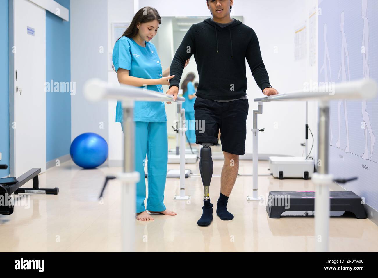 Physiotherapist helping patient with prosthetic leg at parallel bars ...
