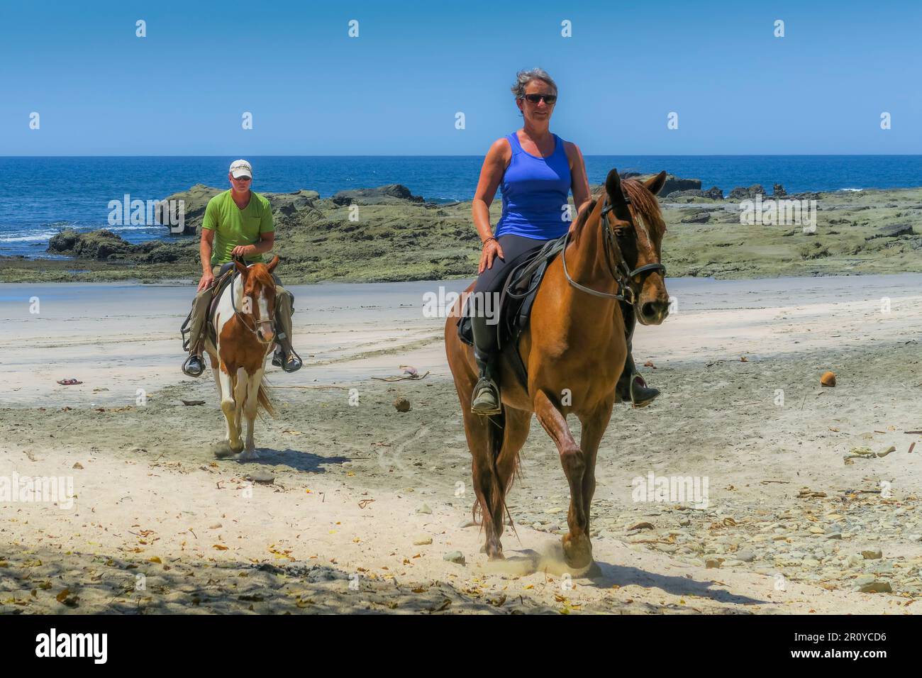 Couple horse riding on lovely Pelada Beach at Nosara, the hip surf & yoga destination. Playa ...