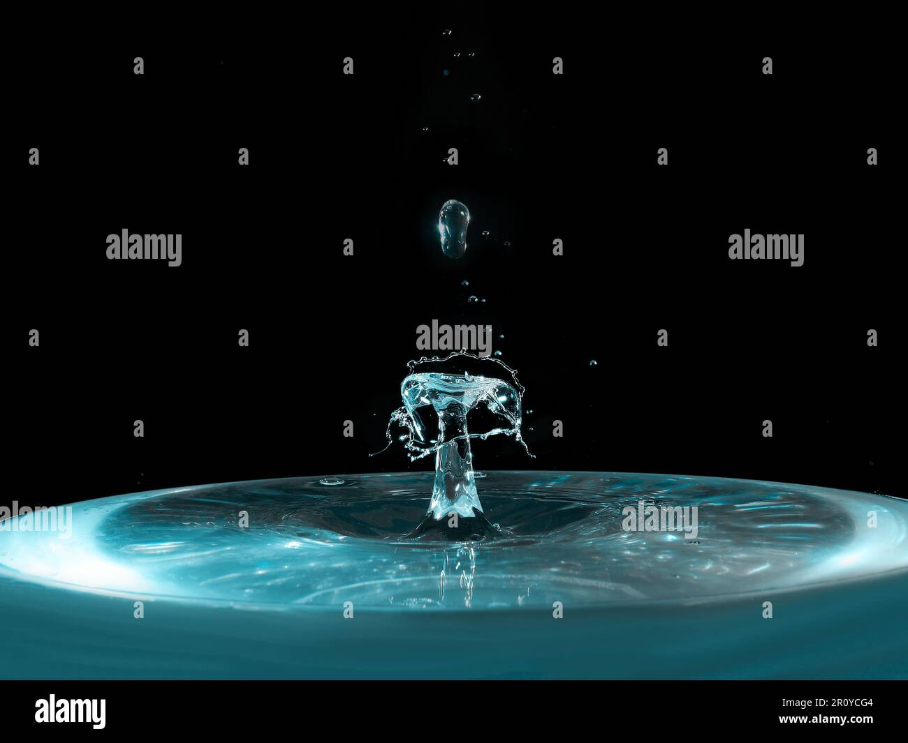 A splash of blue water with a drop flying from above on a dark ...