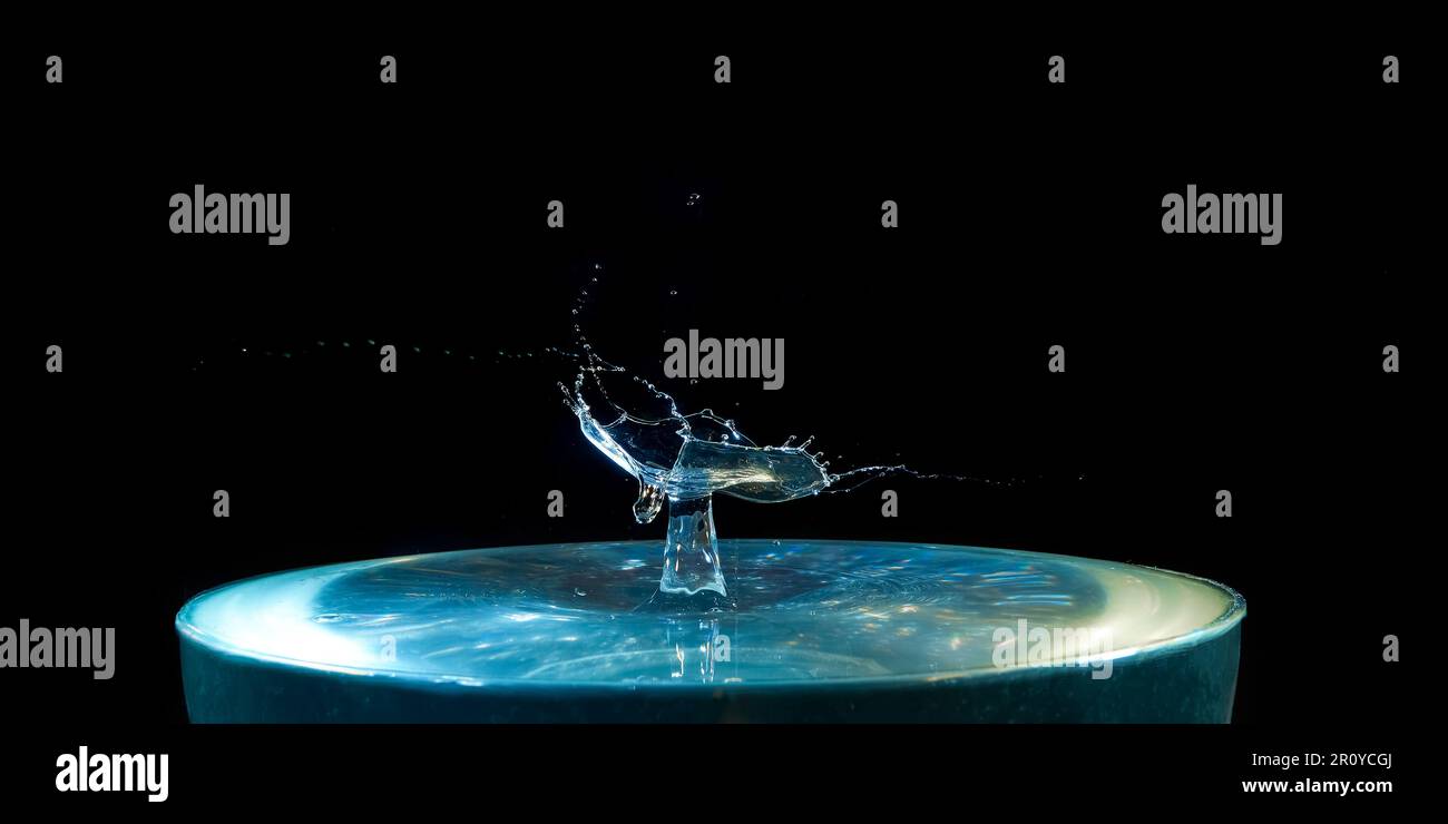 A splash of blue water with a drop flying from above on a dark ...