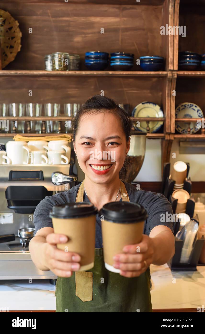Vietnamese smiling waitress holding paper cups with coffee in a cafe ...