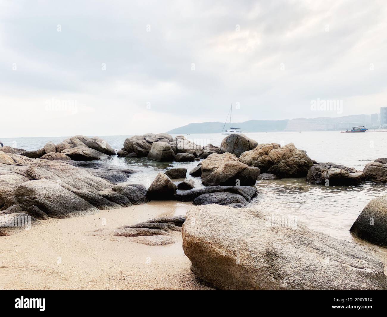 A coastal landscape with a rocky shoreline, two sailboats in the far ...