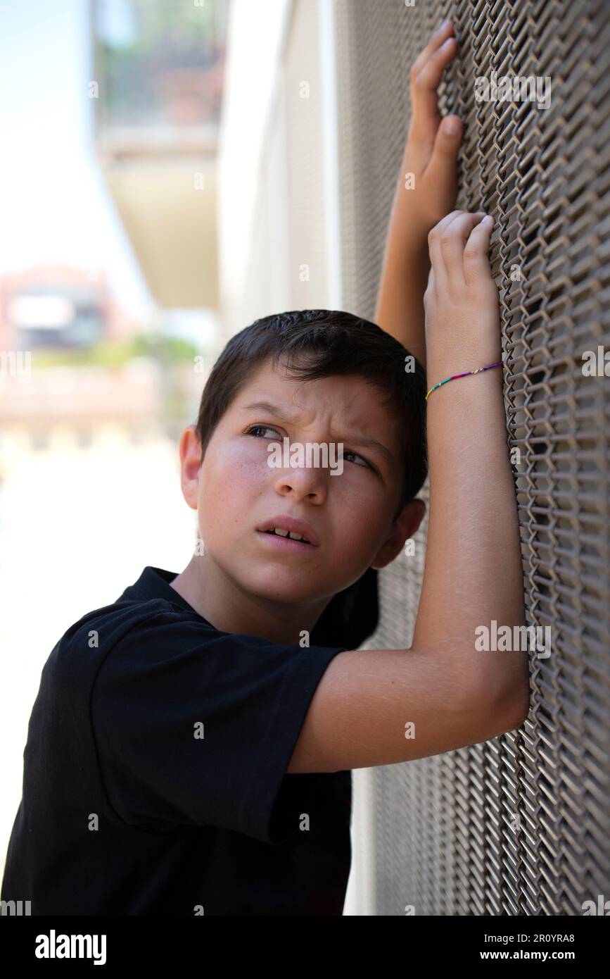 Boy in shorts and black T-shirt leaning on a wall while looking away ...