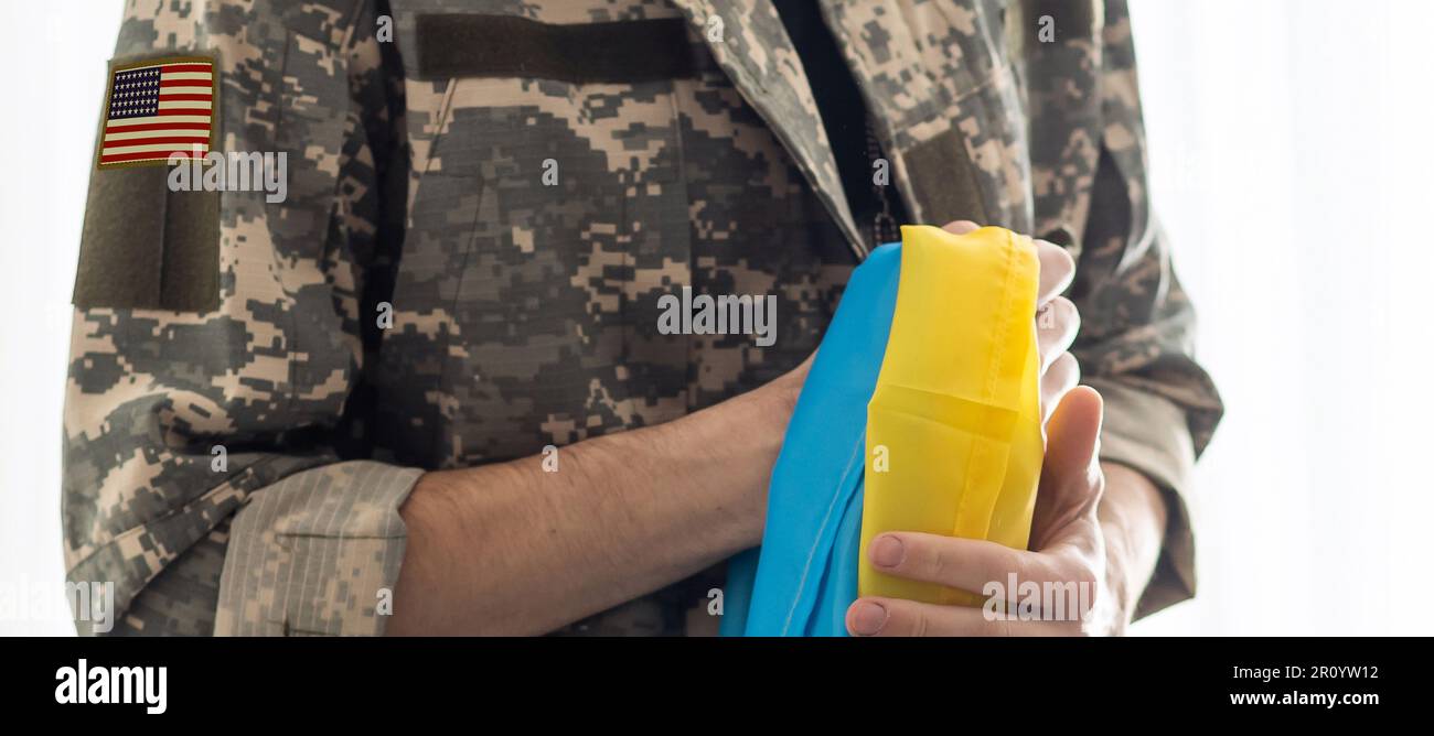 American Flag on Soldiers arm and flag of the Ukraine at background. US ...
