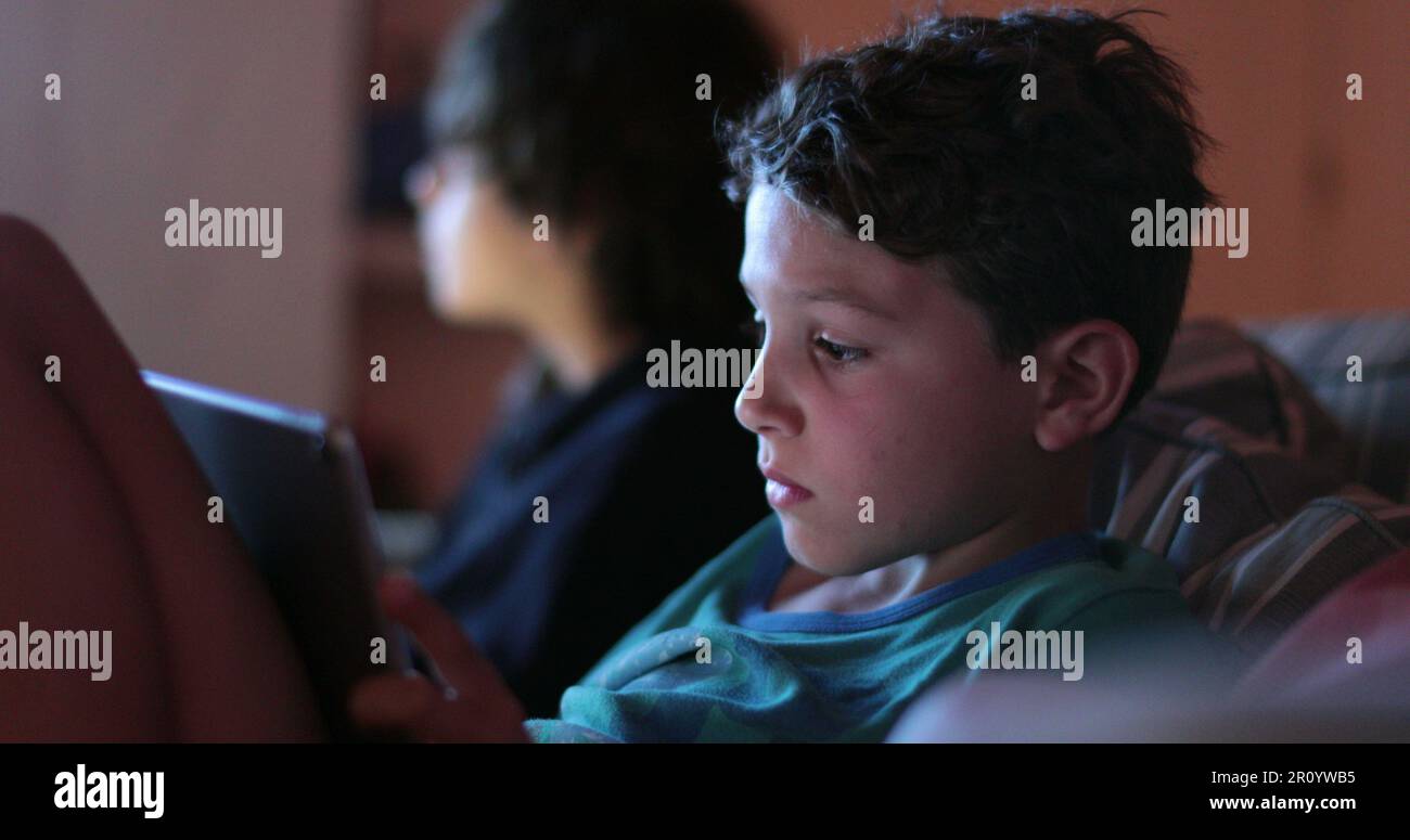 Child watching content on tablet at night. Young boy staring at tech ...