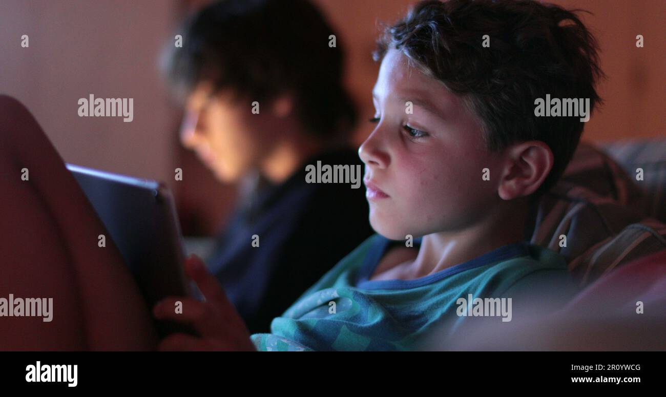Child watching content on tablet at night. Young boy staring at tech ...