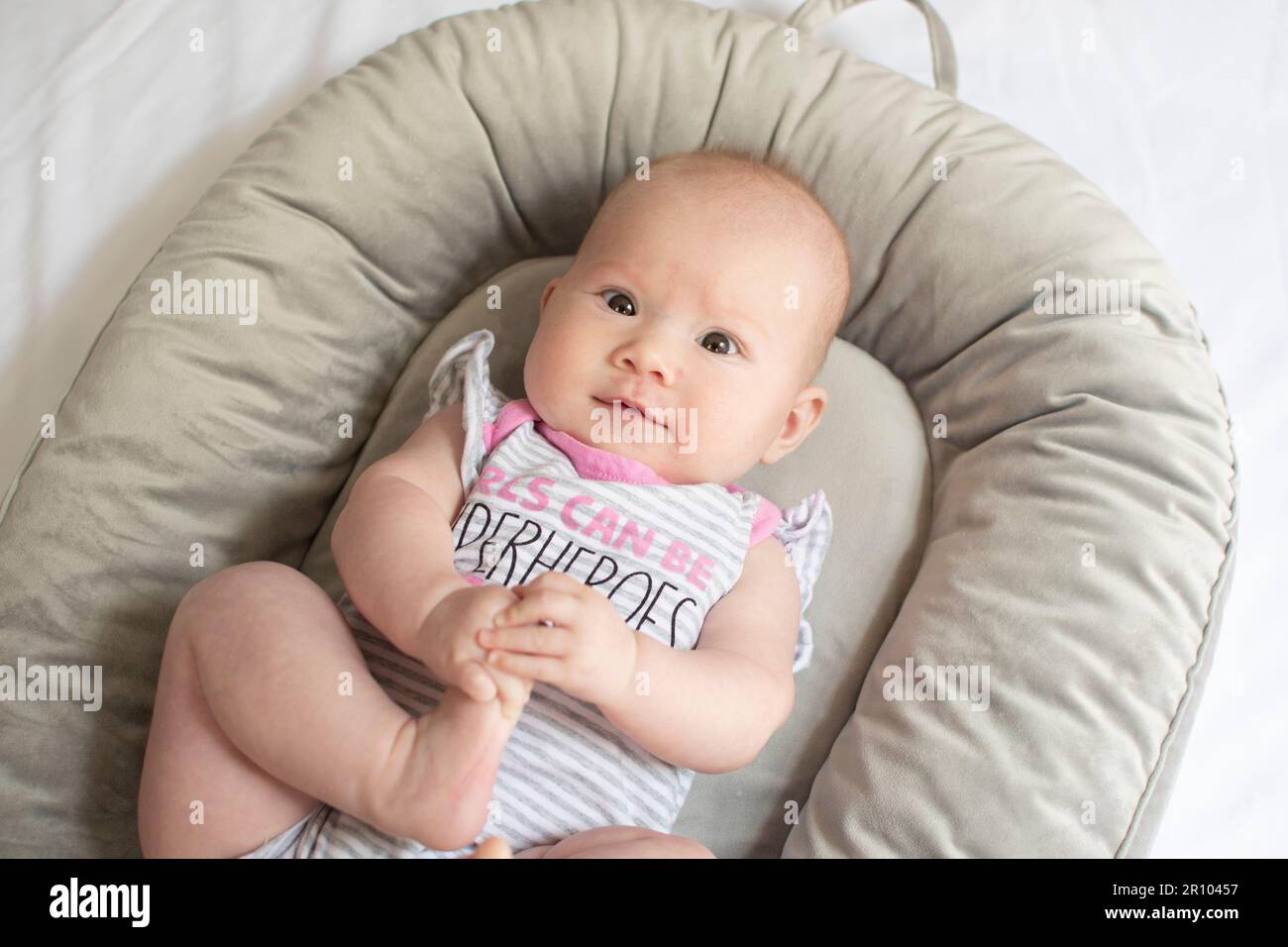 Cute caucasian newborn baby girl in the baby nest playing with her feet. baby milestones Stock ...